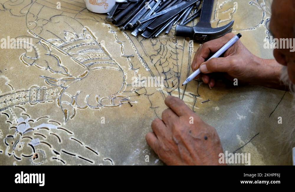 Hands of Thai craftsman drawing Thai pattern on cowhide making Nang Yai ...