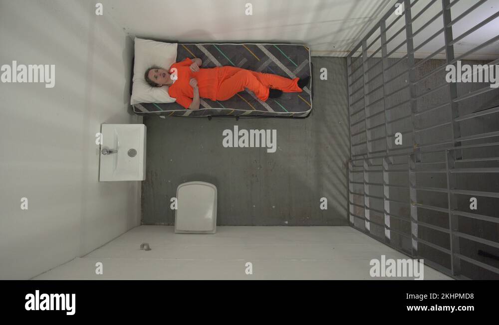 Female Prisoner in Prison Cell. The woman is restless in bed. Overhead ...
