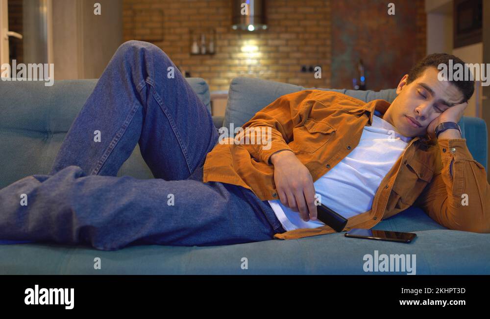 Tired guy watching tv home, yawning and falling asleep on couch late at ...