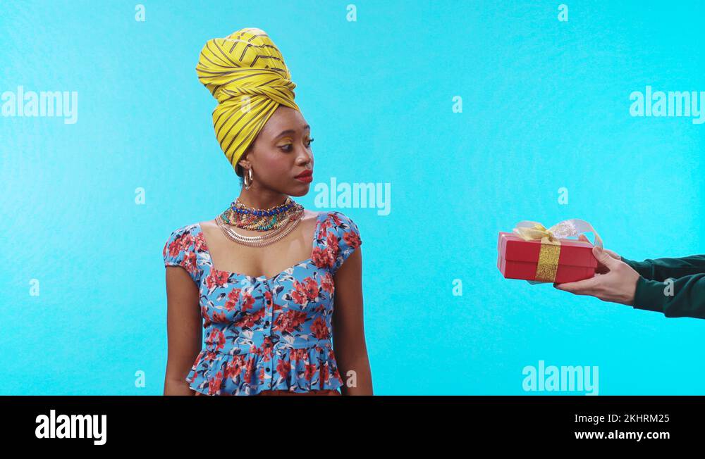 Young beautiful black woman getting a present on holidays shaking box ...