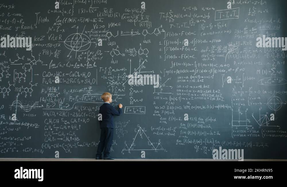 Prodigy child in suit writing formulas on huge blackboard in school ...