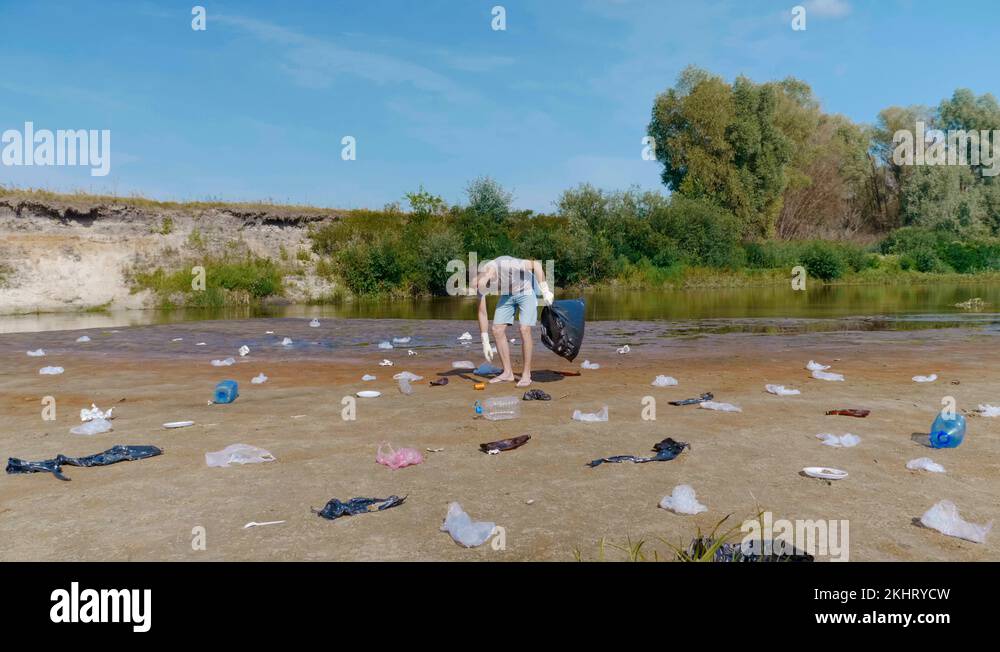 Man collects plastic trash on banks of polluted river and shows thumbs ...