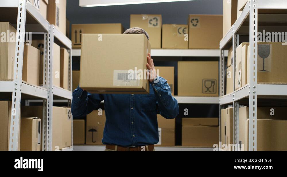 Cheerful Caucasian young postman in uniform and cap holding carton box ...