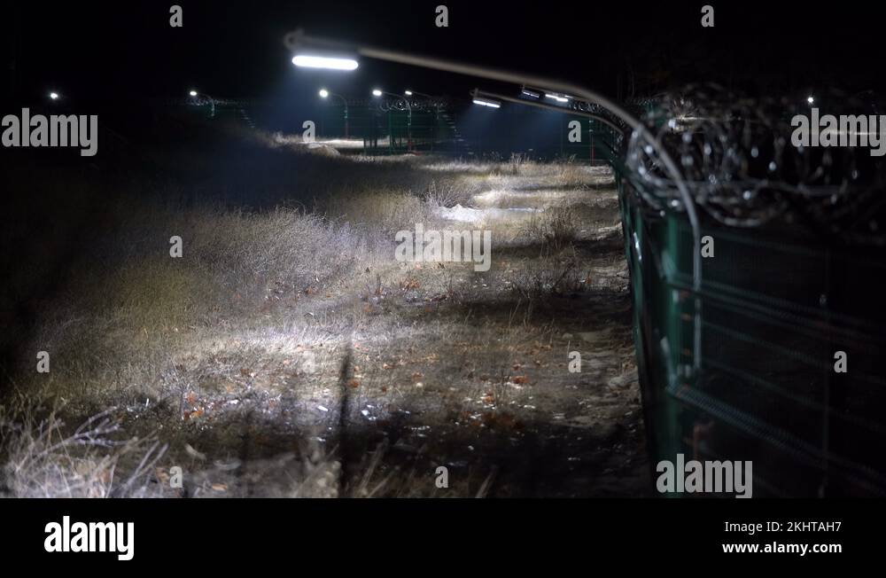 Welded wire mesh fence line with lighting and razor wire at night Stock ...