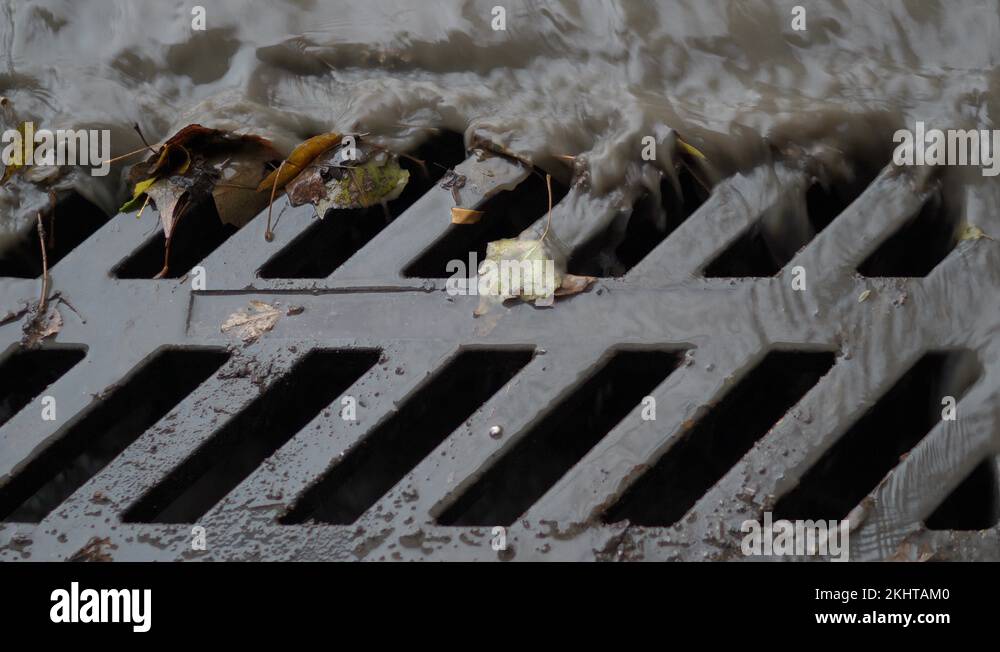 Rain water with debris flows down storm drain at the side of a street ...