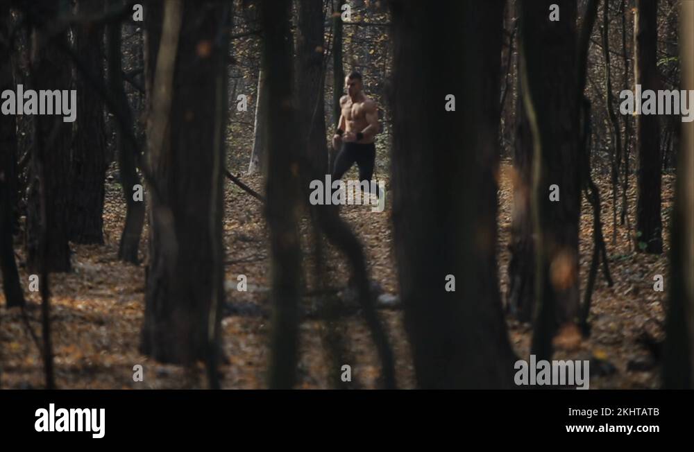 lonely muscular athlete runs in the forest between the trees with naked ...