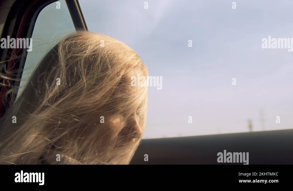 Woman looks out open car window as blond hair swirls across face, close ...