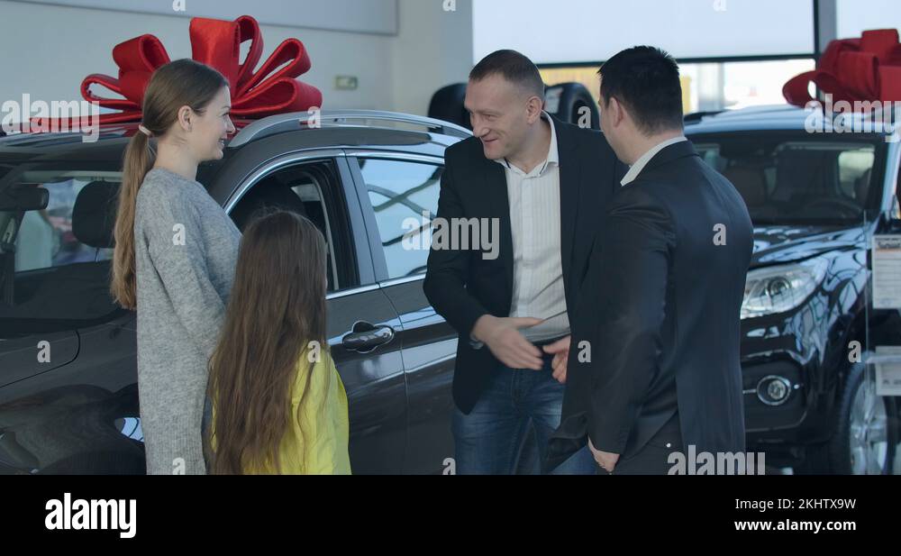 Positive Caucasian car dealer welcoming young couple with daughter in ...