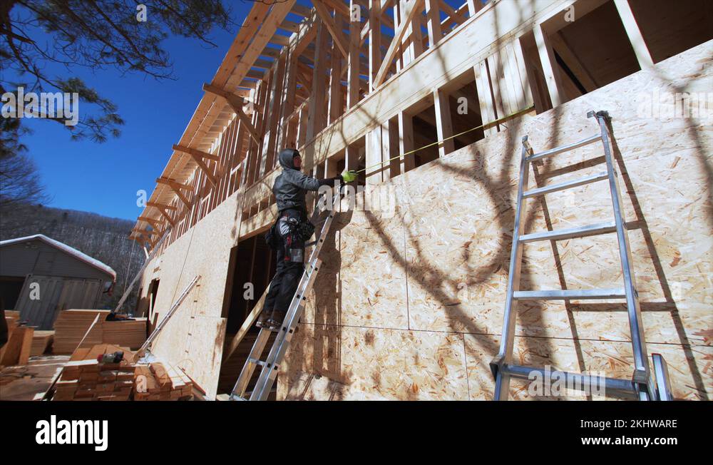 Builders on ladders measure plywoods with measuring tape.Frame house ...