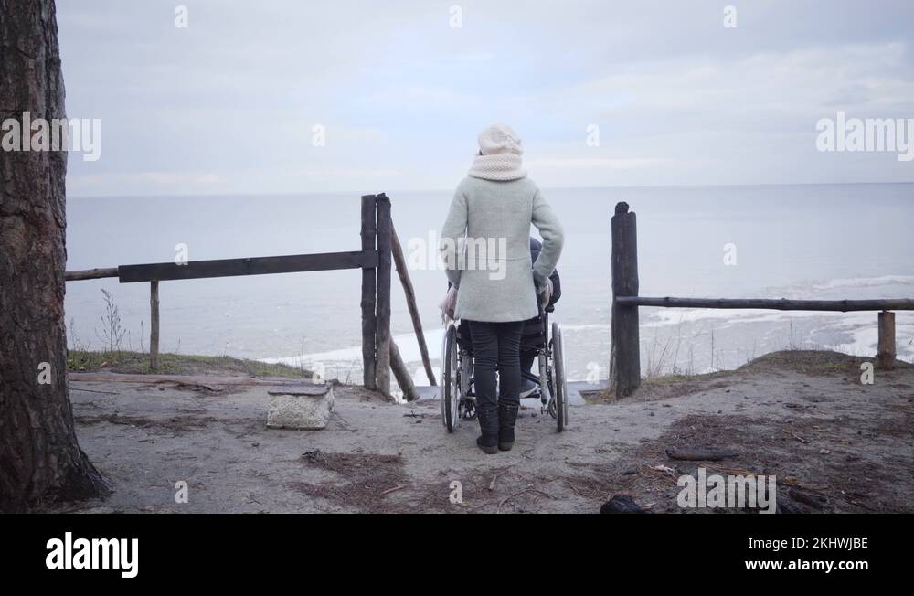 Back view of female invalid tender standing with disabled man in ...