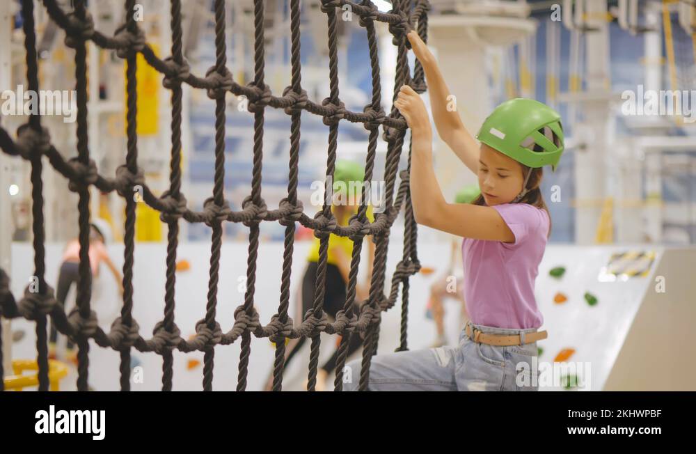 Teenage girl crawling on rope mesh at playground in amusement park ...
