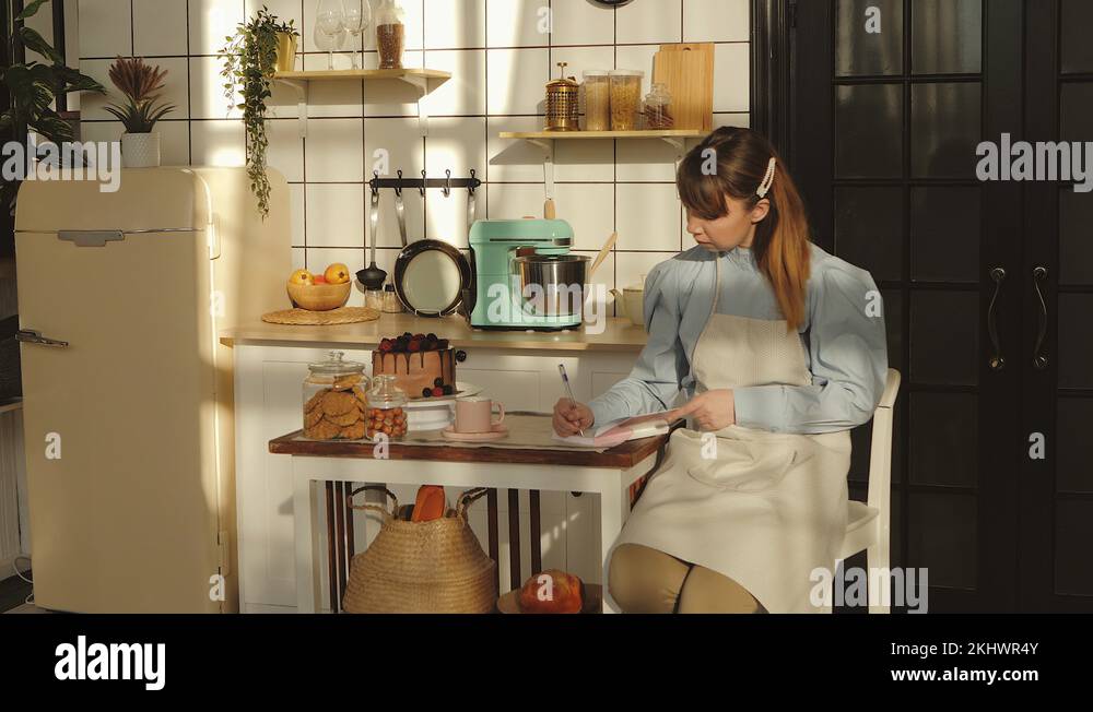 Beautiful woman is making notes while cooking in the kitchen Stock ...