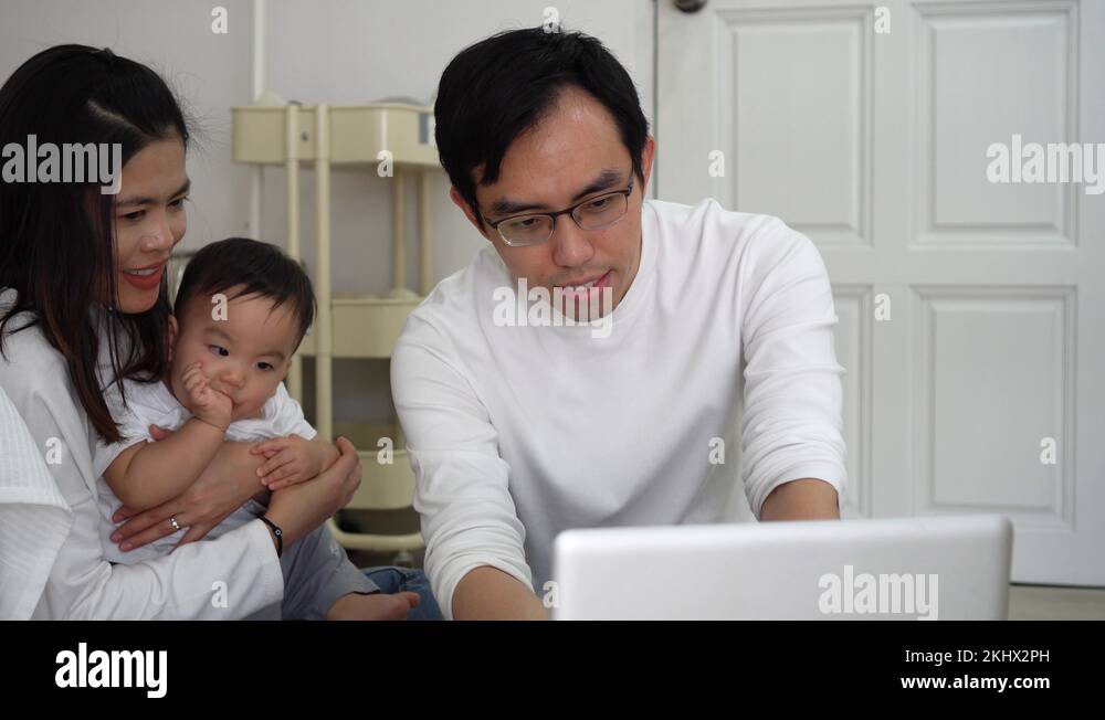 Asian father working using laptop with his wife and cute Asian baby boy ...
