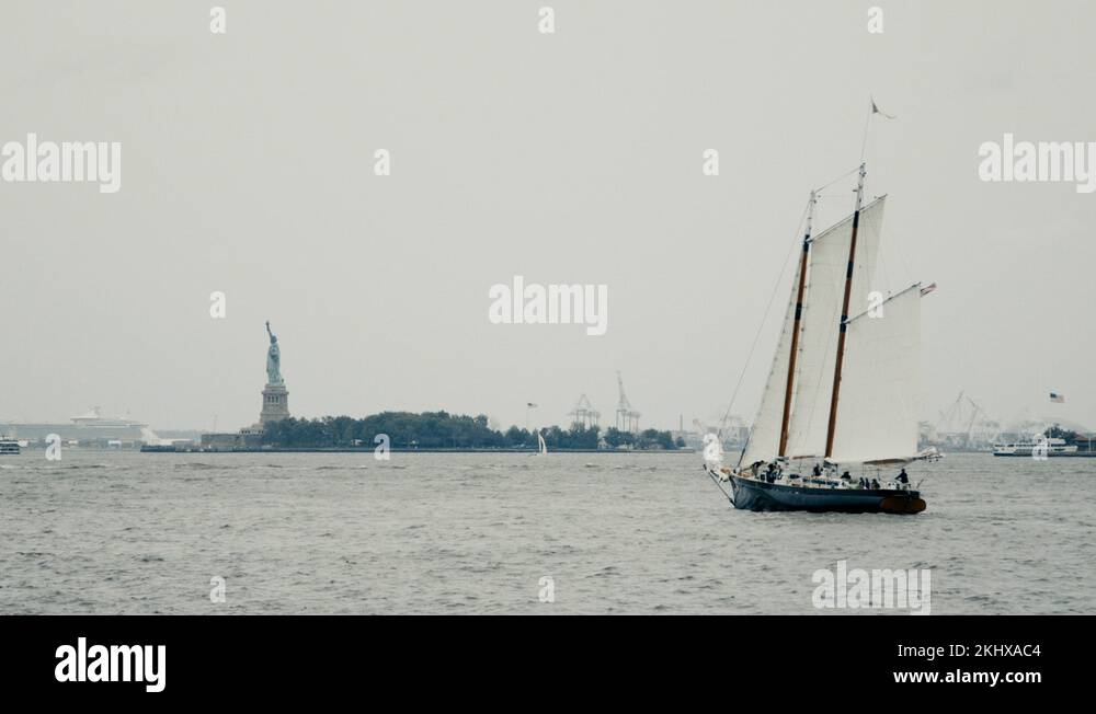 Statue of Liberty and Liberty Island in background as sail boat passes ...