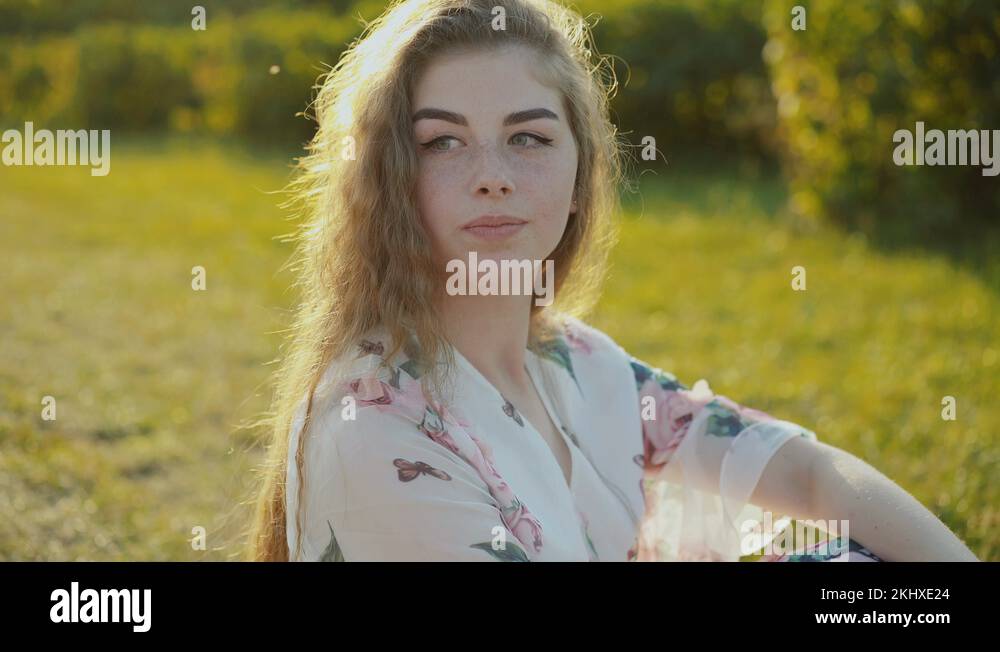 Beautiful curly-haired lady wore in dress relaxes and smiles on nature ...