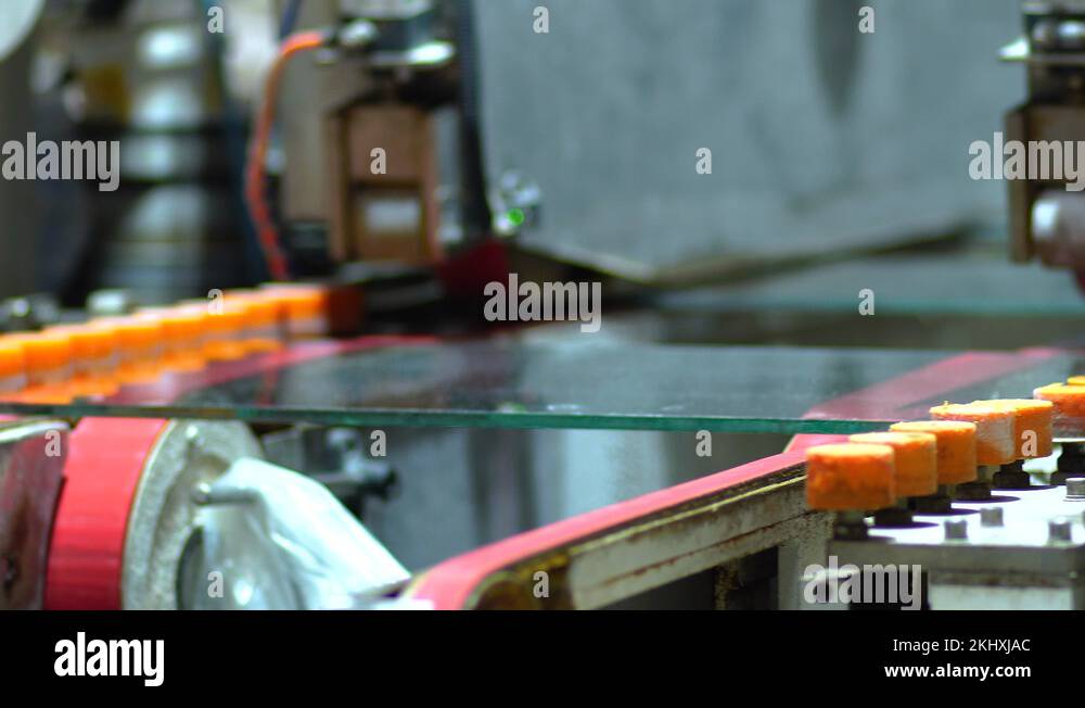 A sheet of glass on a conveyor belt in a glass grinding machine. Glass ...