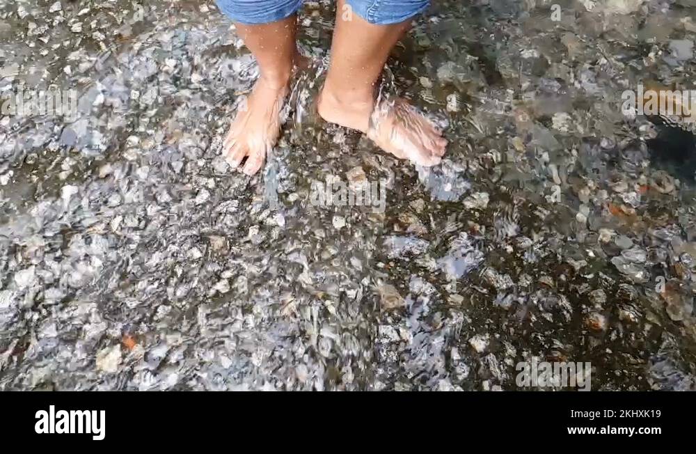 feet of a lady wearing jeans dipped and splashing water in slow motion ...