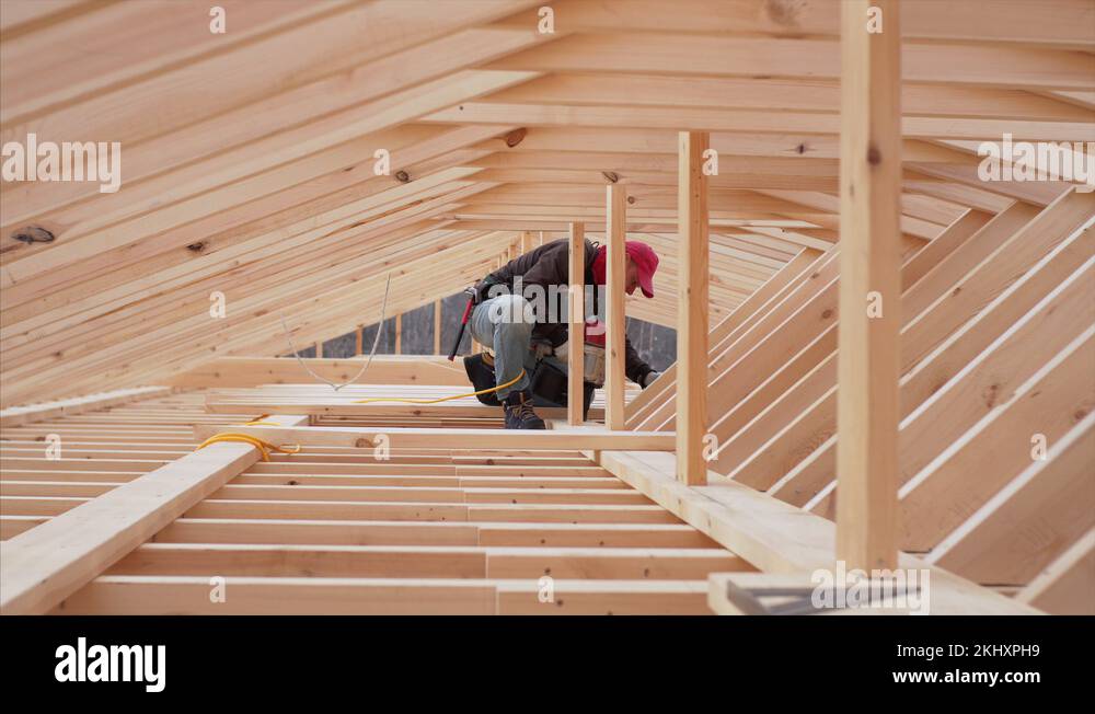 Builder works on the frame house attic nailing planks with pneumatic ...