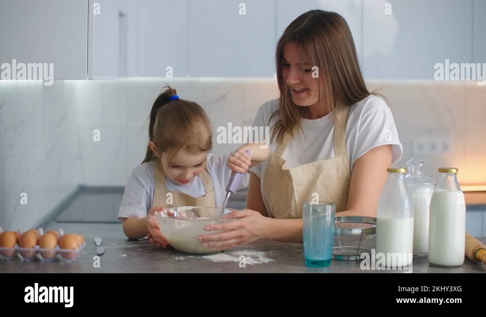 Laughing mom and daughter are cooking in the kitchen. The girl learns from her Stock Video ...