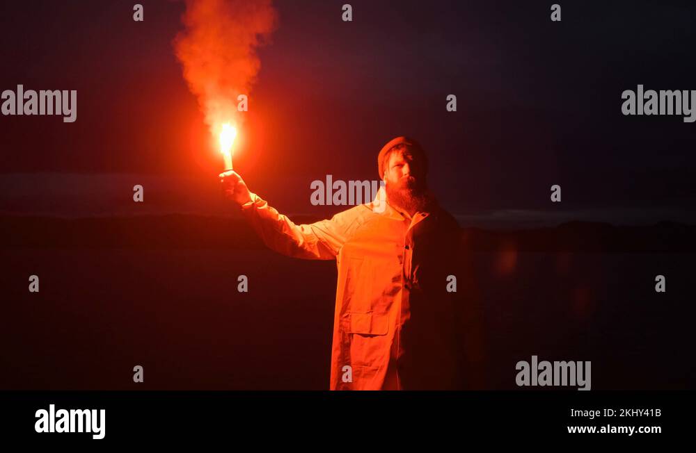 man raincoat,waving red smoke signal,light, lake mountains.traveler ...