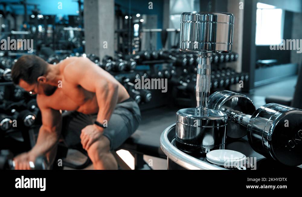 A man bodybuilder pumping his hand muscles sitting in the sports gym ...