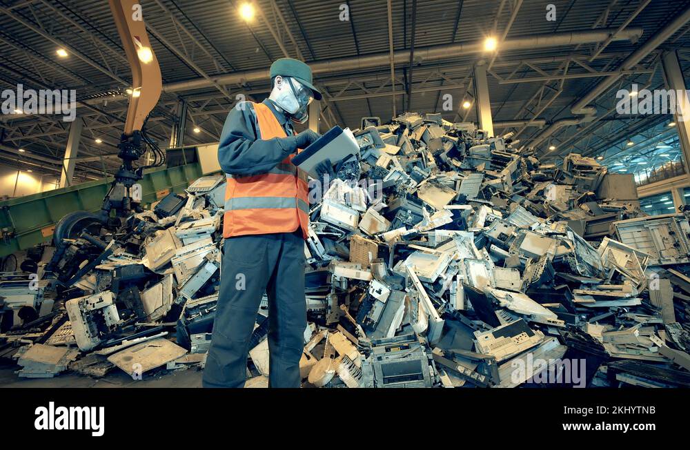 A pile of broken equipment in a dumpsite with a male worker. Garbage ...