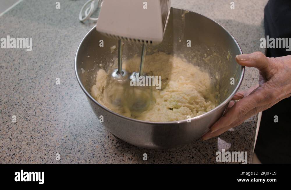 Female chef using vintage electric hand mixer in stainless steel mixing ...