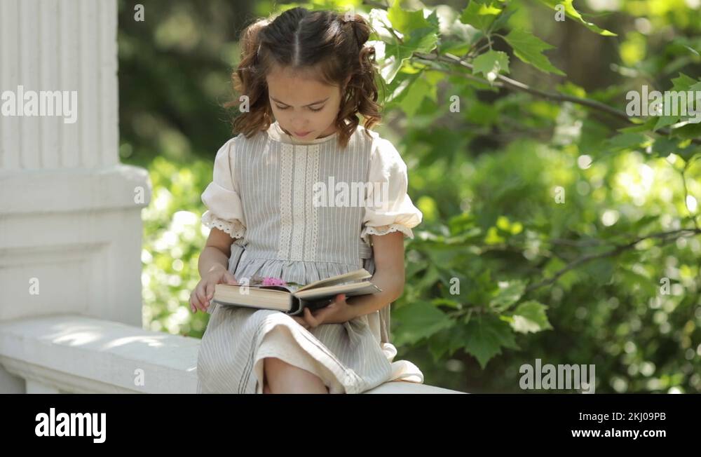 A girl in a school uniform sits on concrete steps and reads a book ...