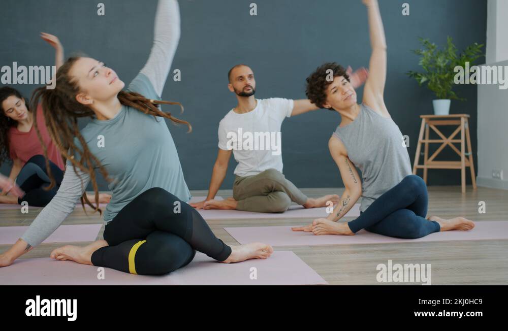 Female yoga trainer speaking showing Gomukhasana position to group of ...
