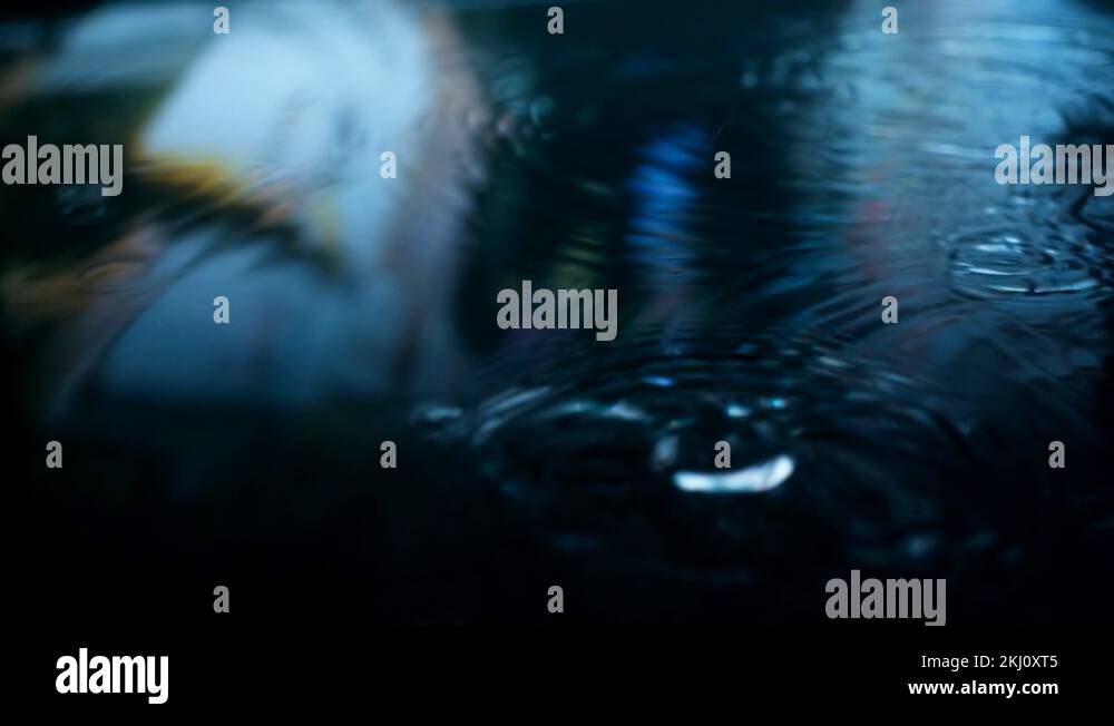 Rain drops falling into puddle. City street reflection on water surface ...