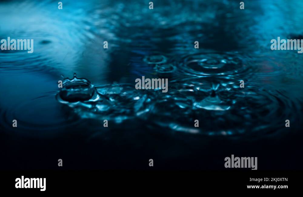 Rain drops falling into puddle on asphalt at night. Big city lights ...