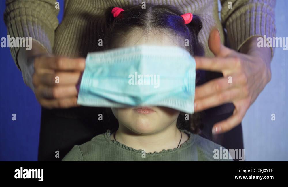 Mother putting on face of her little cheerful daughter surgical mask ...