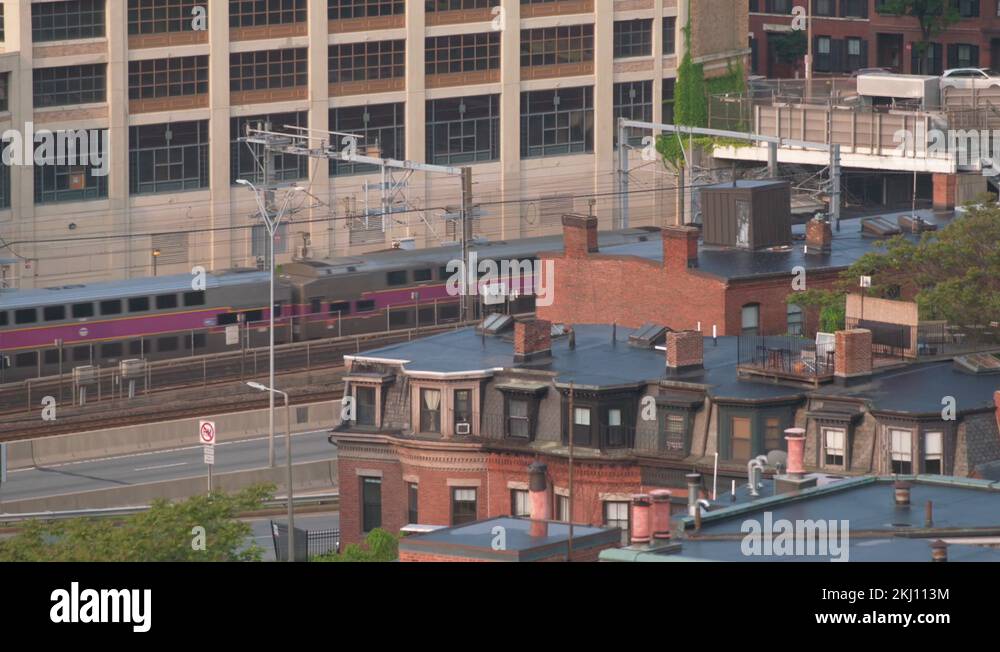 A two story passenger train passes between an industrial factory and a ...