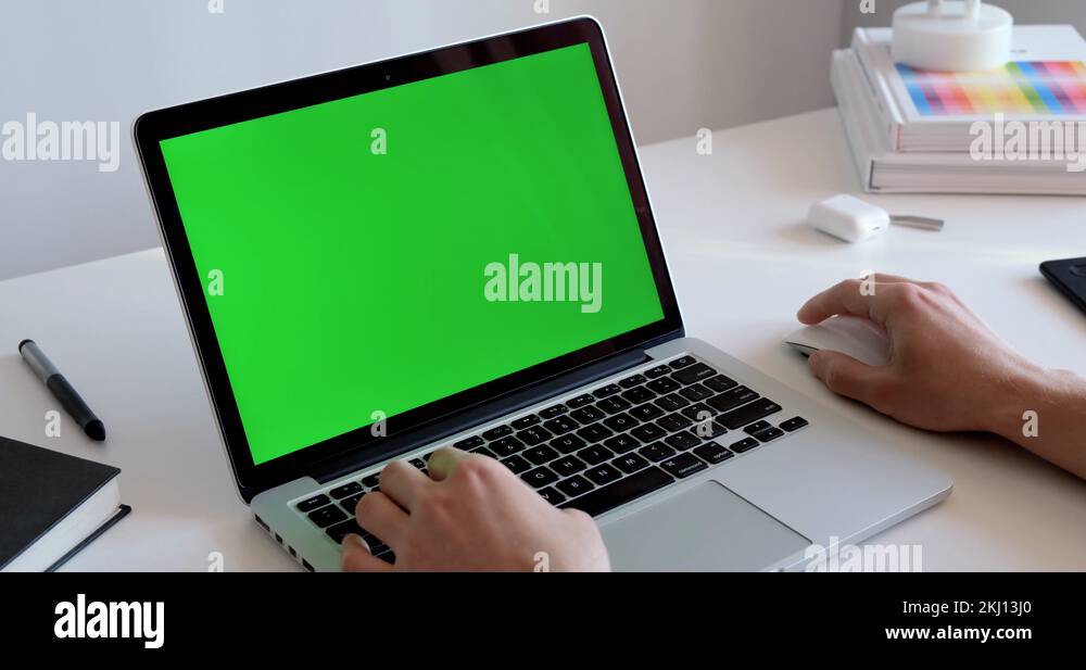 Man working in front of a laptop in a white modern office with a green ...