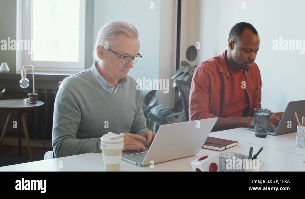 Young Black Man Helping Senior Colleague with Using Laptop at Work ...