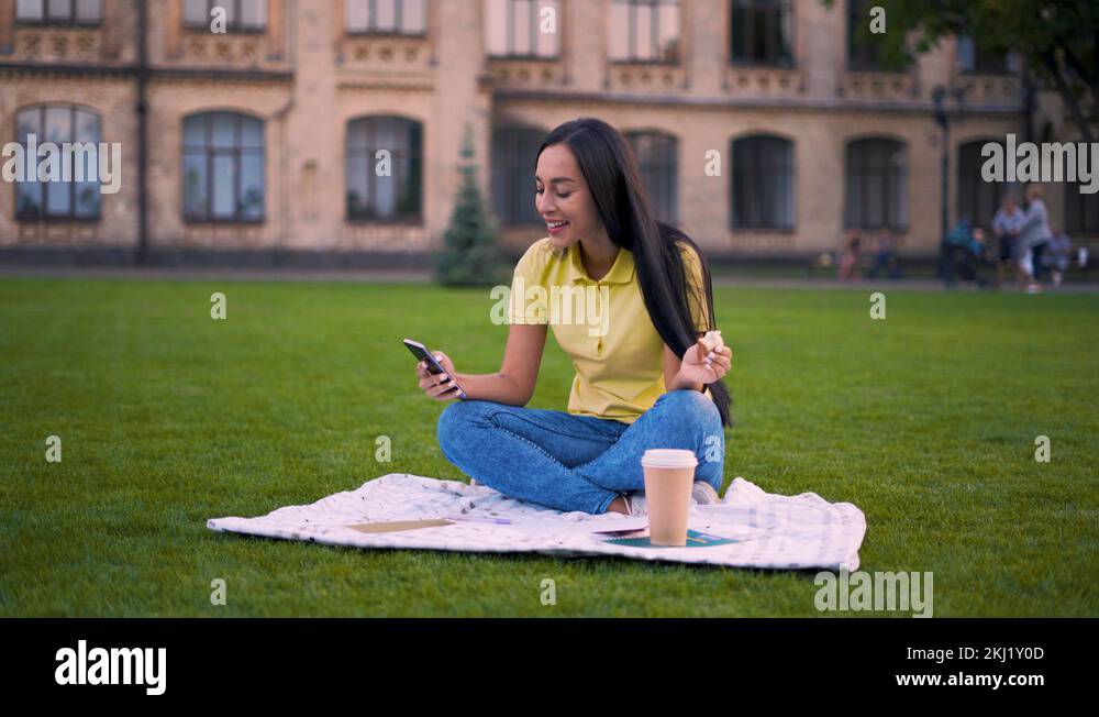 cheerful girl on a picnic. Girl scrolls the phone laughs and eats a ...