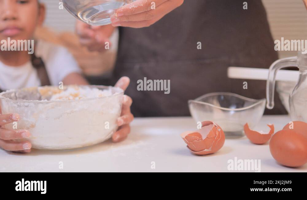 Mother pouring the water into a mixing bowl with flour to mix in the ...