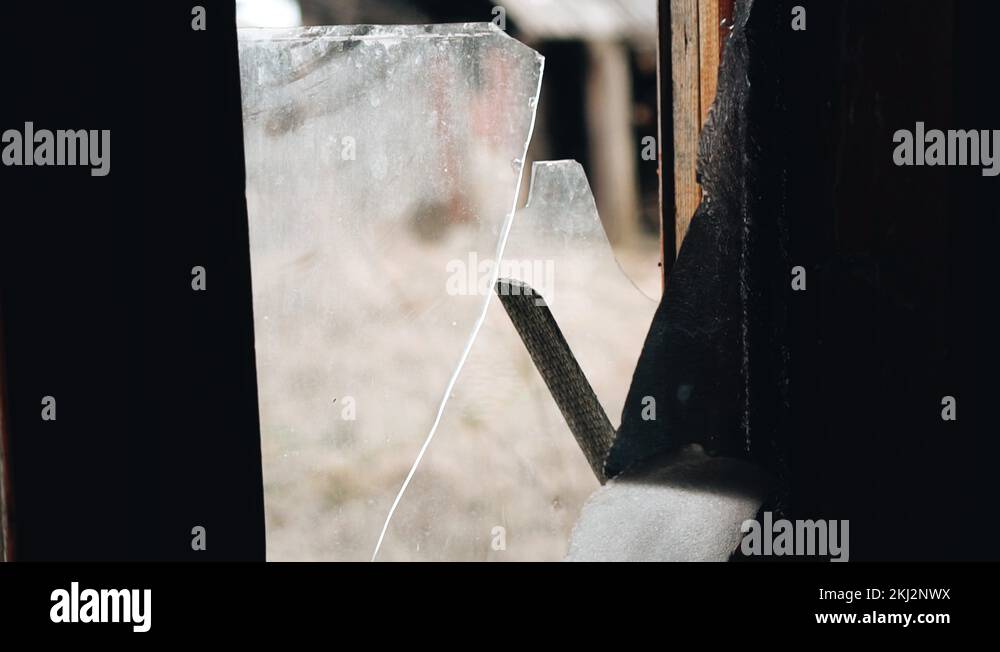 The boy removes the broken glass from the window frame. Abandoned house ...