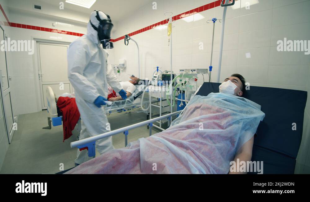 Doctor in a hazmat suit is checking temperature of a lying patient ...