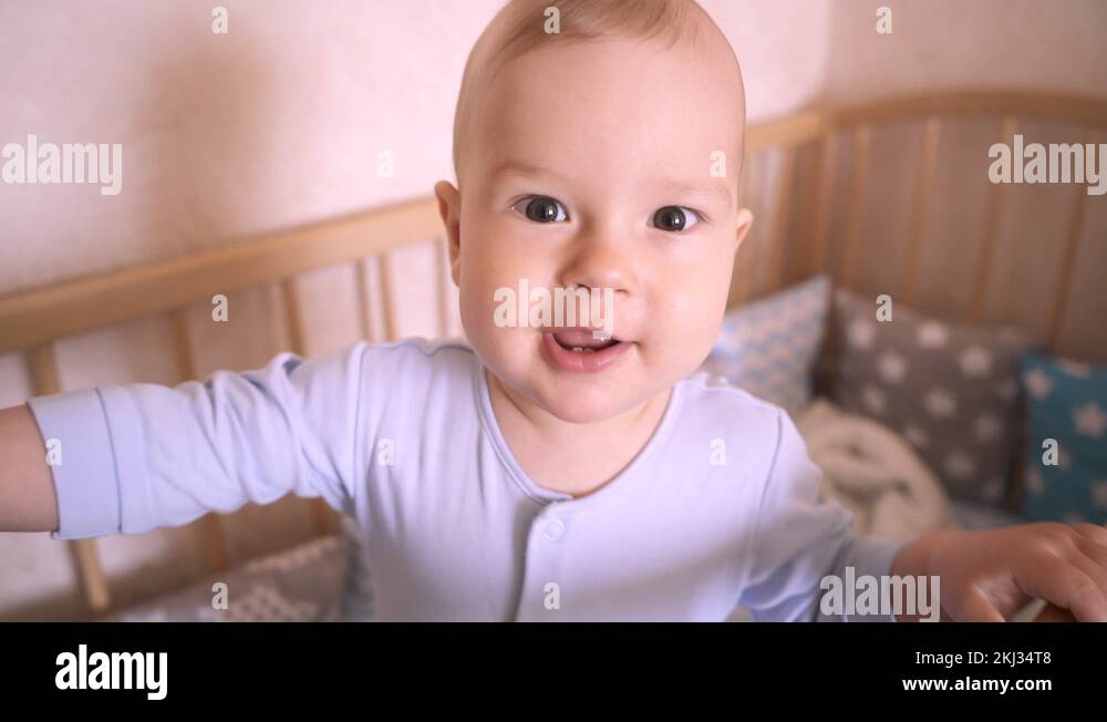 Funny Baby Stands In Bed And Looks At Camera. Child Stretches Hands ...