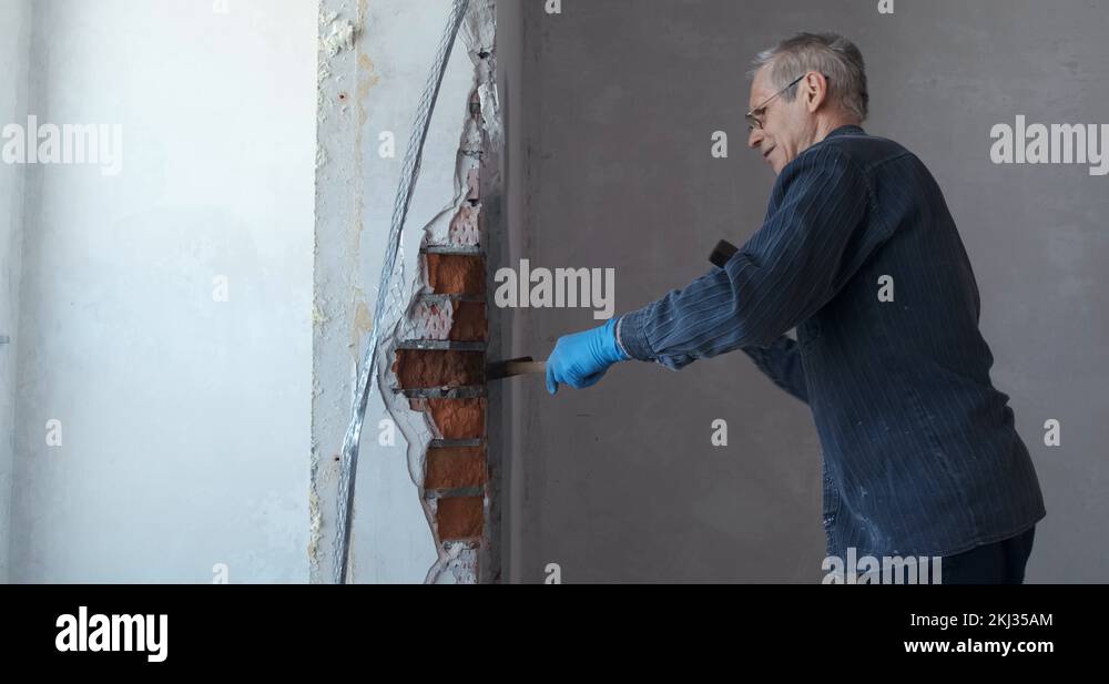 Builder smashes a brick wall with hammer. Plaster and bricks fall in ...