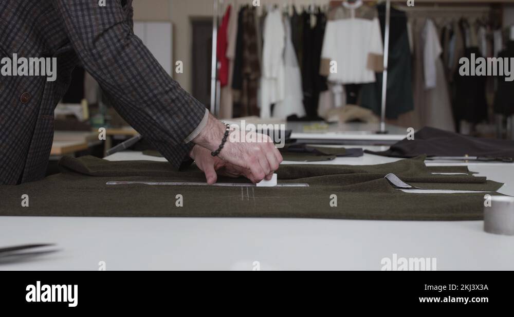 The tailor draws the markings on a fabric with chalk on desktop in ...