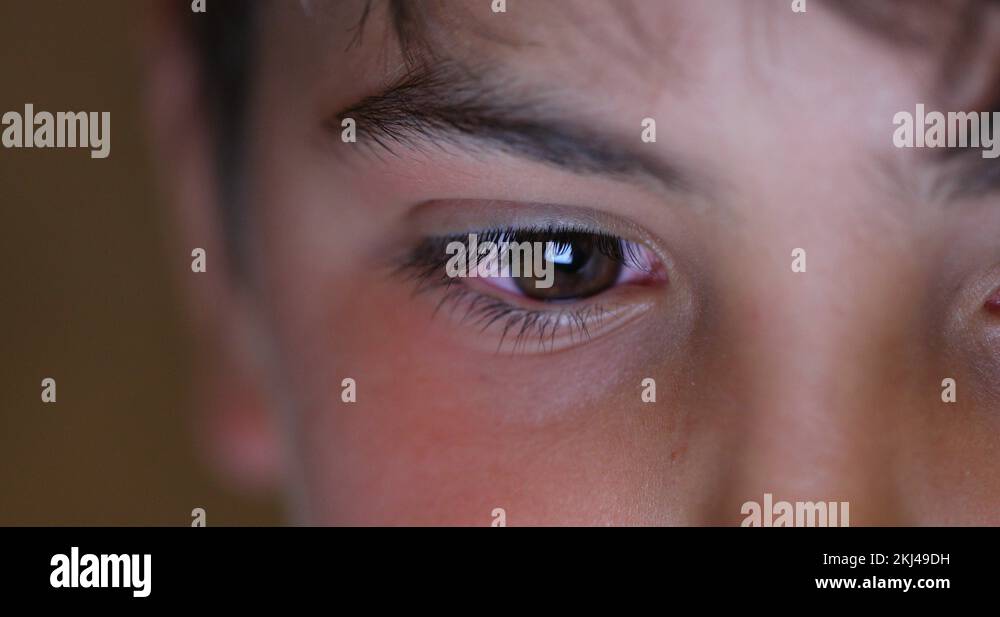 Young boy eyes staring at screen at night. Close-up of child face ...