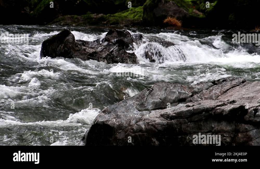 Fast water flows past and over a granite outcropping in a wild and ...
