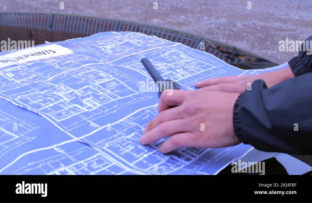 Man planning entry into building using blueprints on car hood. The man ...