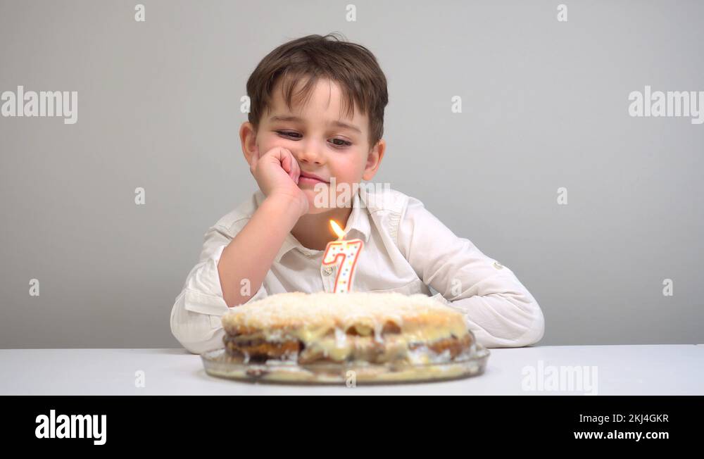 Sad boy looks to a cake with lighting candles on his birthday Stock ...