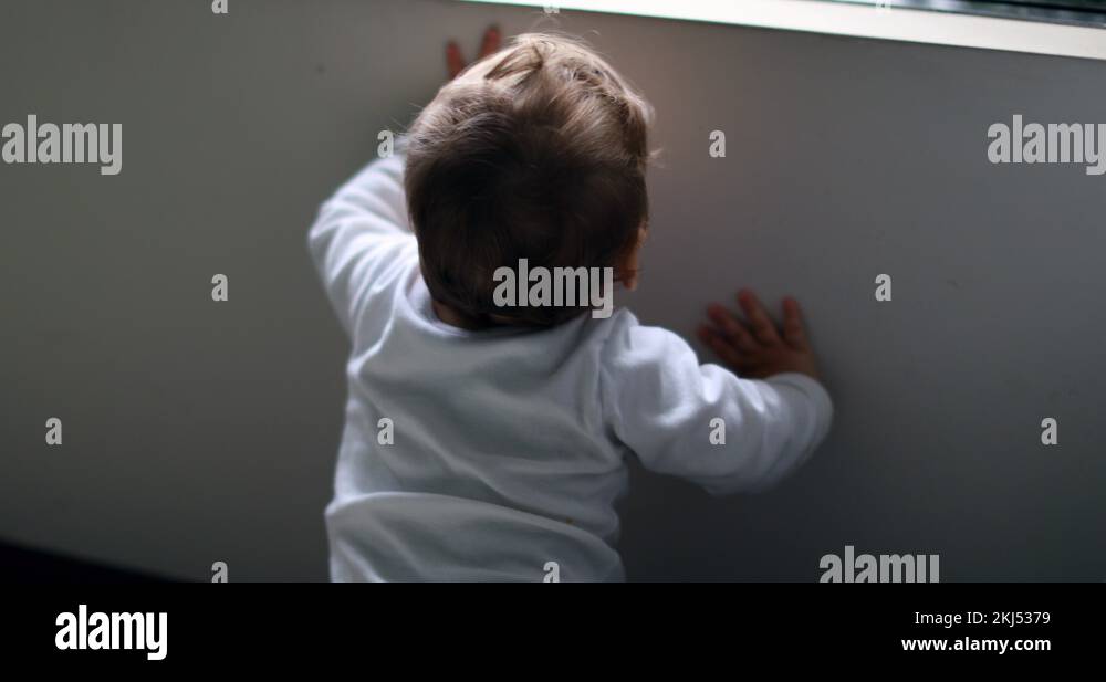 Adorable baby learning to stand by leaning on window looking outside ...