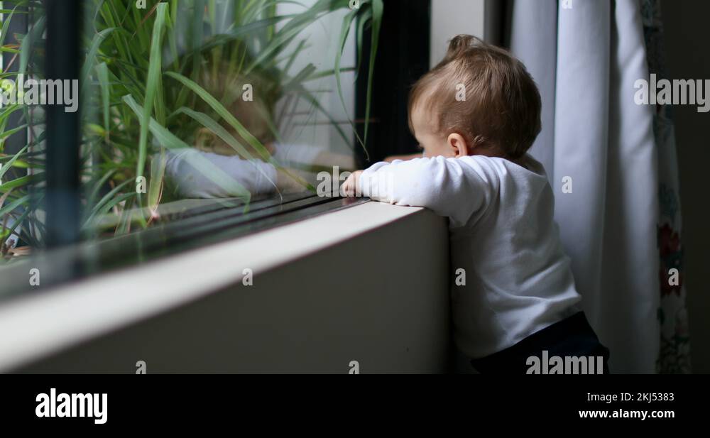 Adorable baby learning to stand by leaning on window looking outside ...