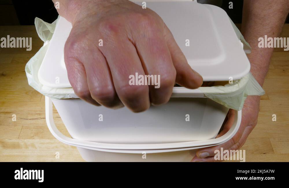 Man placing food waste into kitchen composting bin fitted with ...