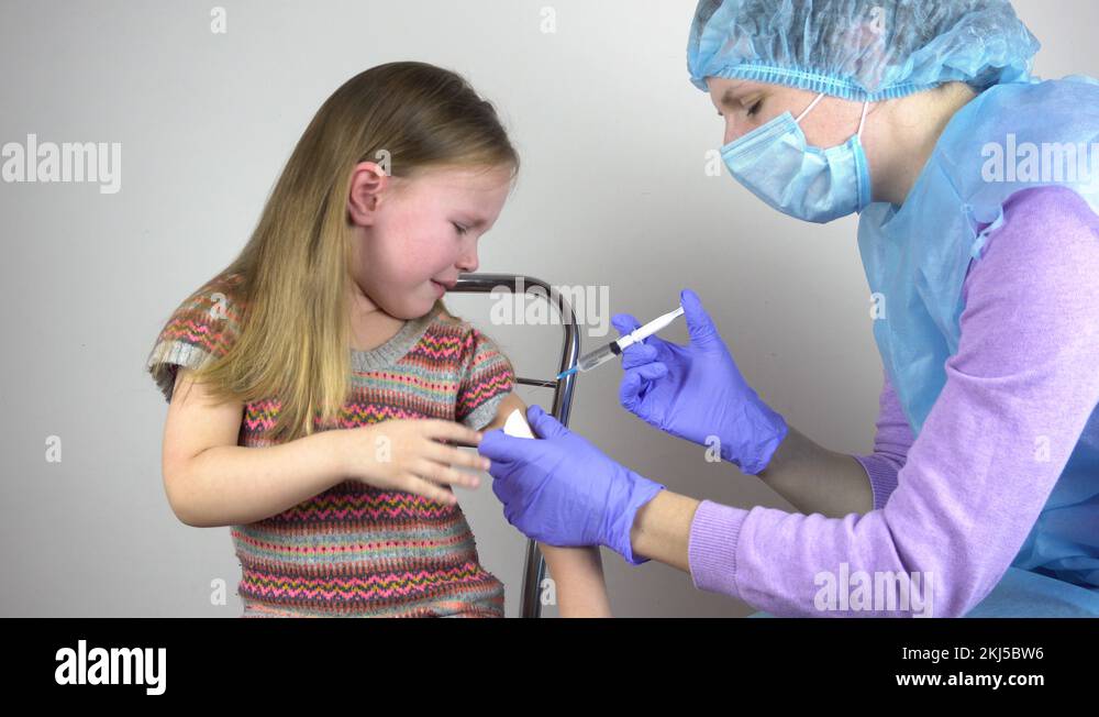 A doctor injects a vaccine to a little girl. The girl is afraid and ...